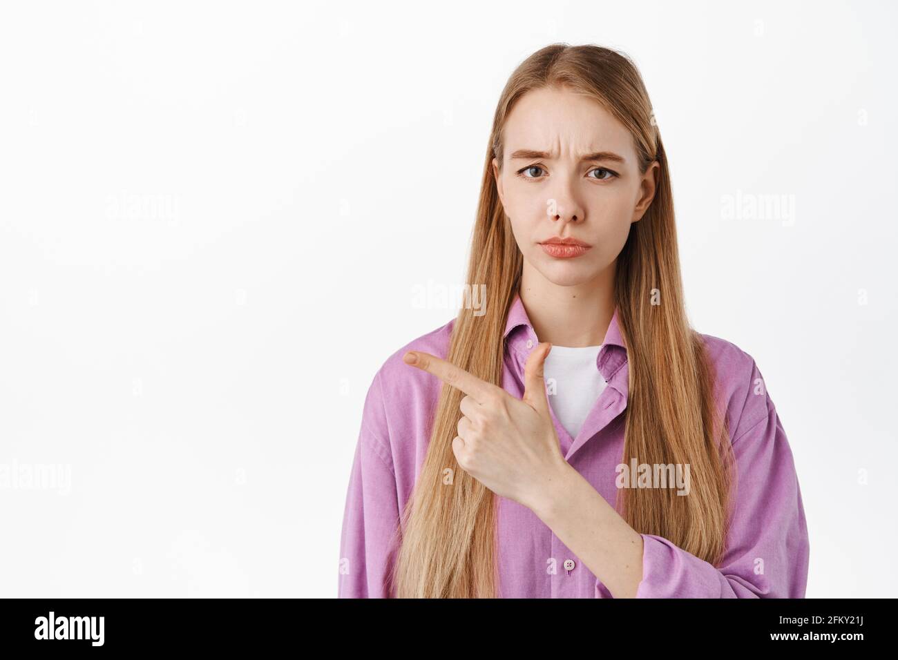 Close up of sad and disappointed blond girl pointing finger left ...