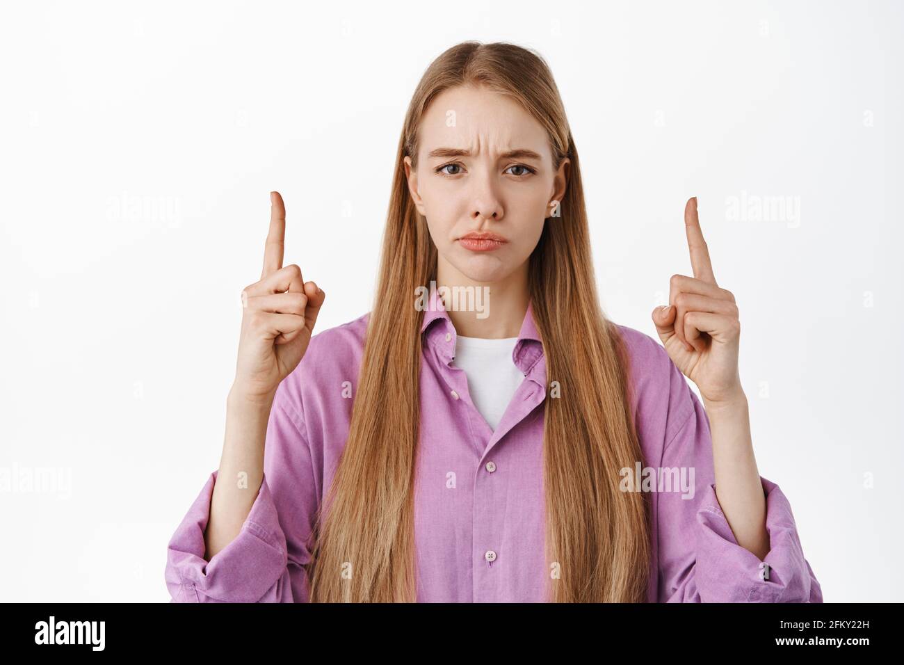 Close up portrait of disappointed female pointing fingers up, grimacing ...