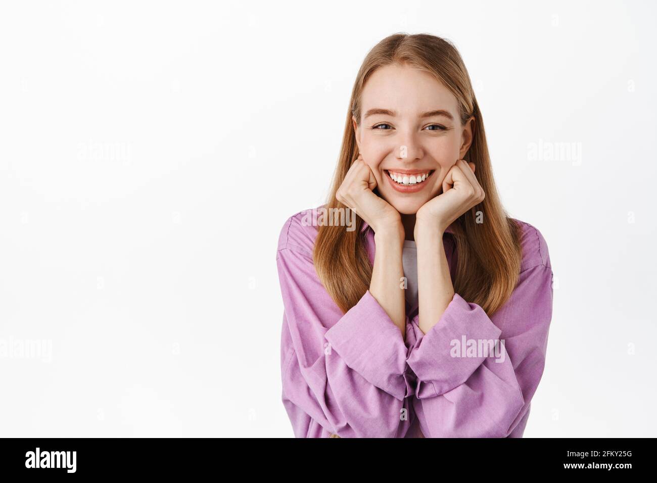 Beautiful blond girl touching face, looking at something adorable ...