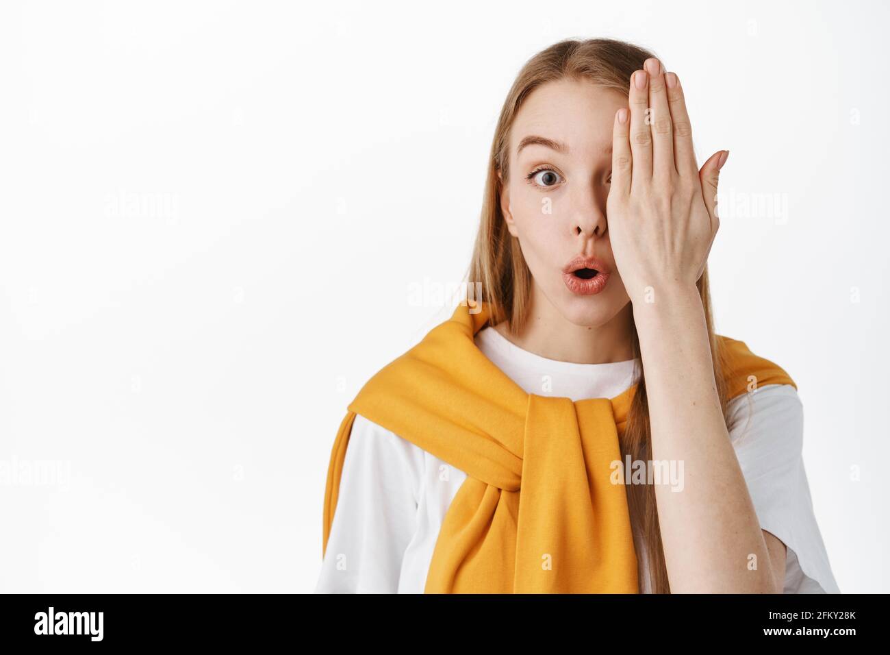Close up portrait of blond girl covering half of face, looking with one ...