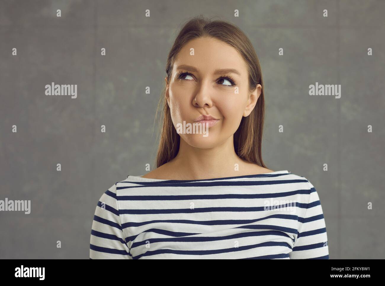 Studio portrait of young doubtful woman looking up thinking or planning ...