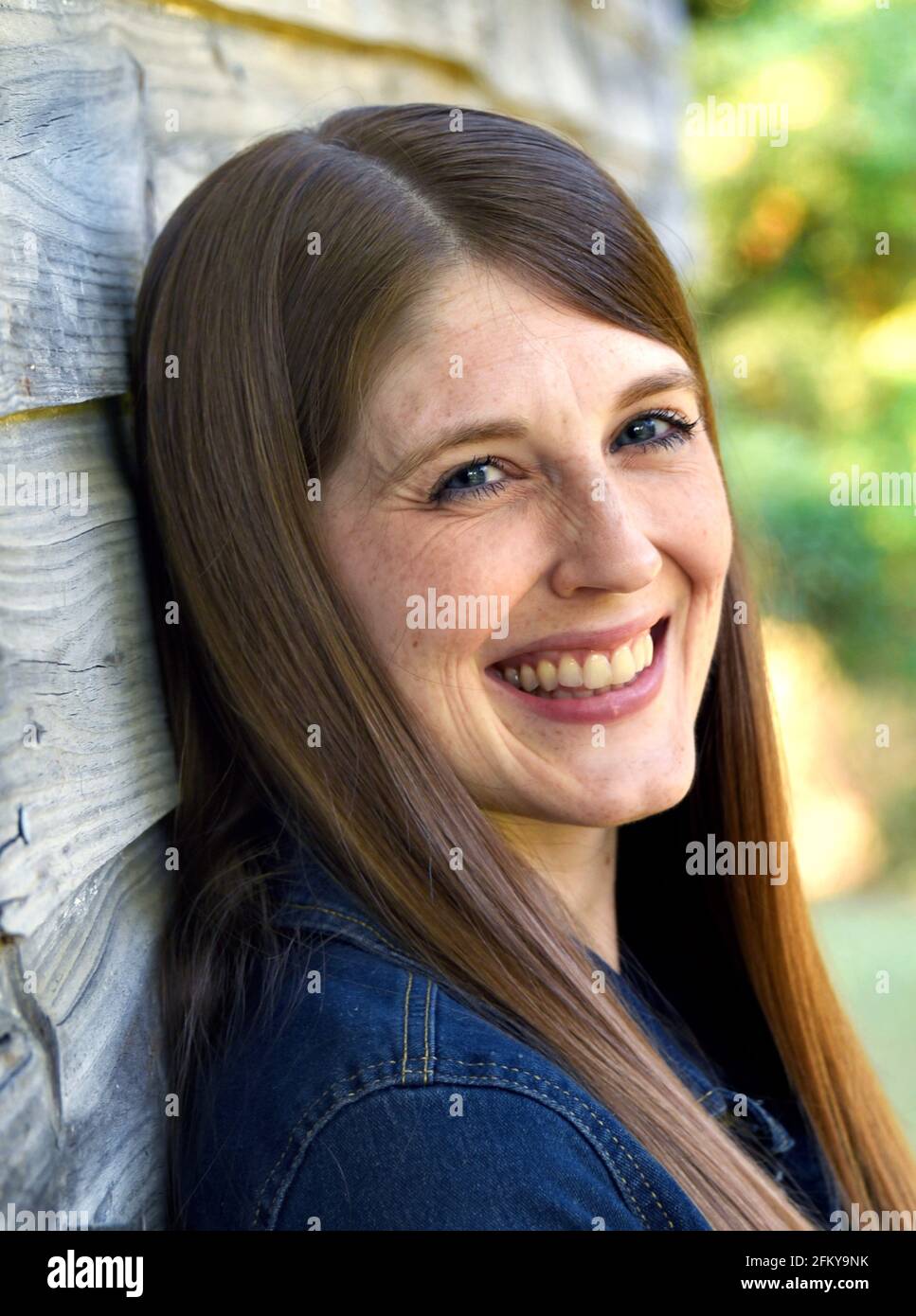 Young woman leans her head against a wooden building and beams the ...