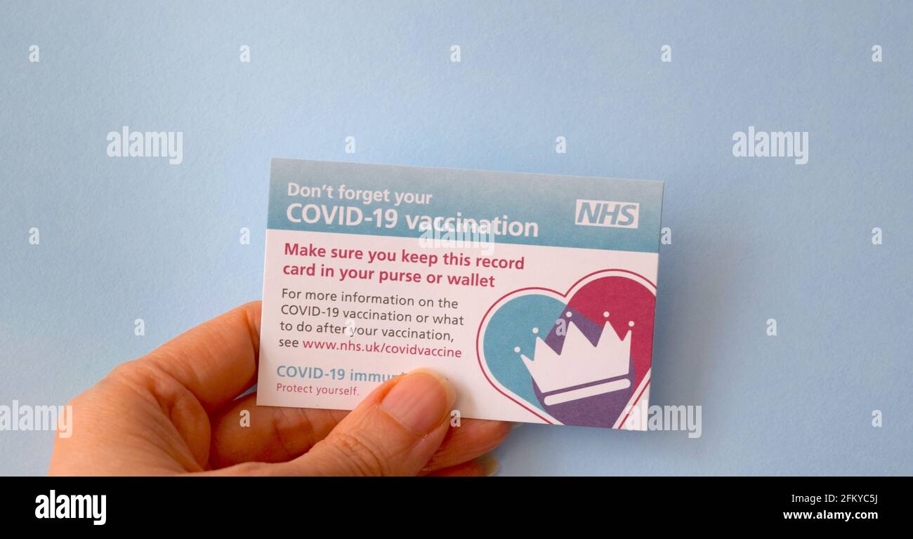 NHS Covid-19 vaccination card in female hand on blue Stock Photo - Alamy