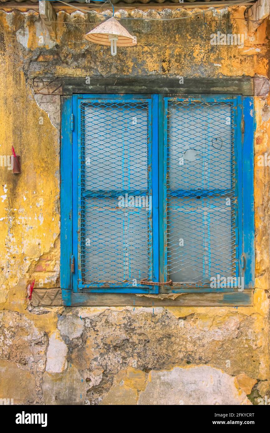 A blue window frame against a decaying traditional yellow Vietnamese ...