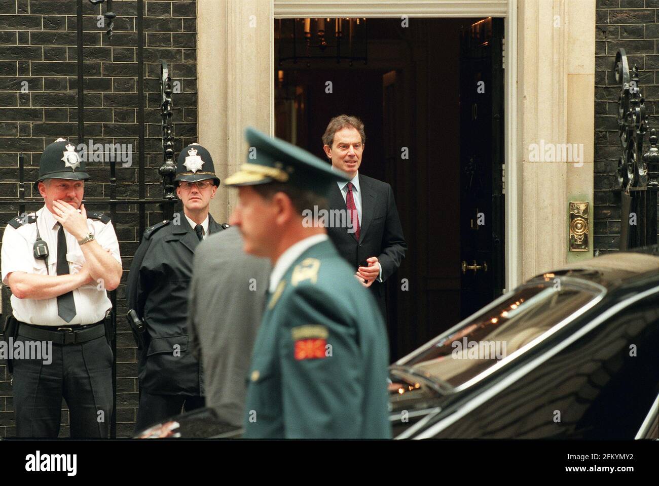 Tony Blair standing by car wearing grey/black suit red tie police ...