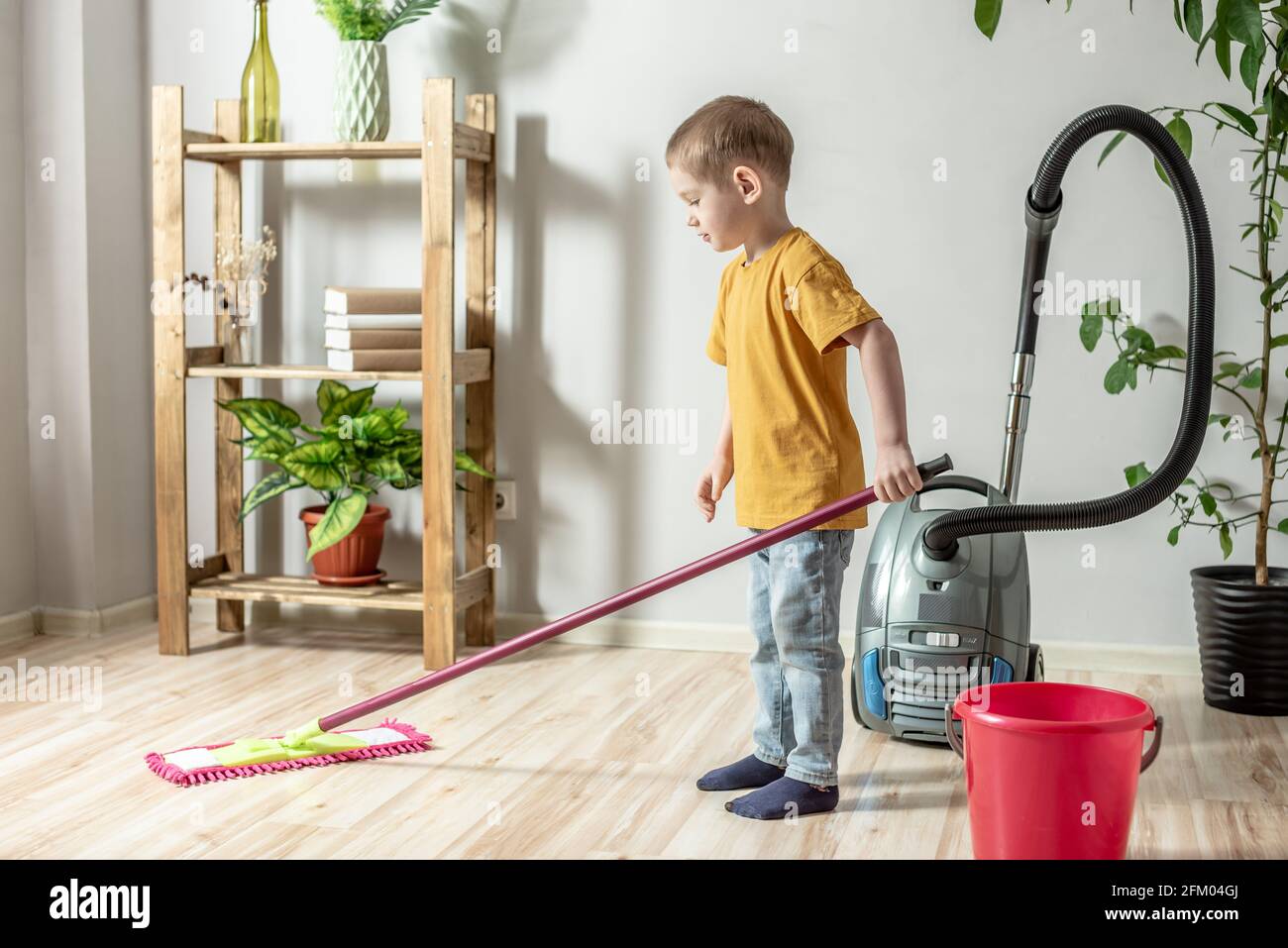 A little boy is cleaning the floor of a room using a mop. Concept of ...