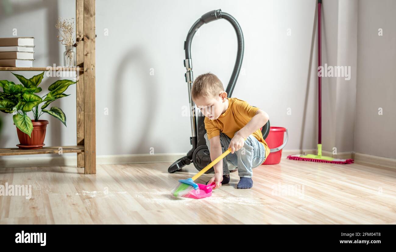 A cute little boy helps in cleaning the house by sweeping the garbage ...