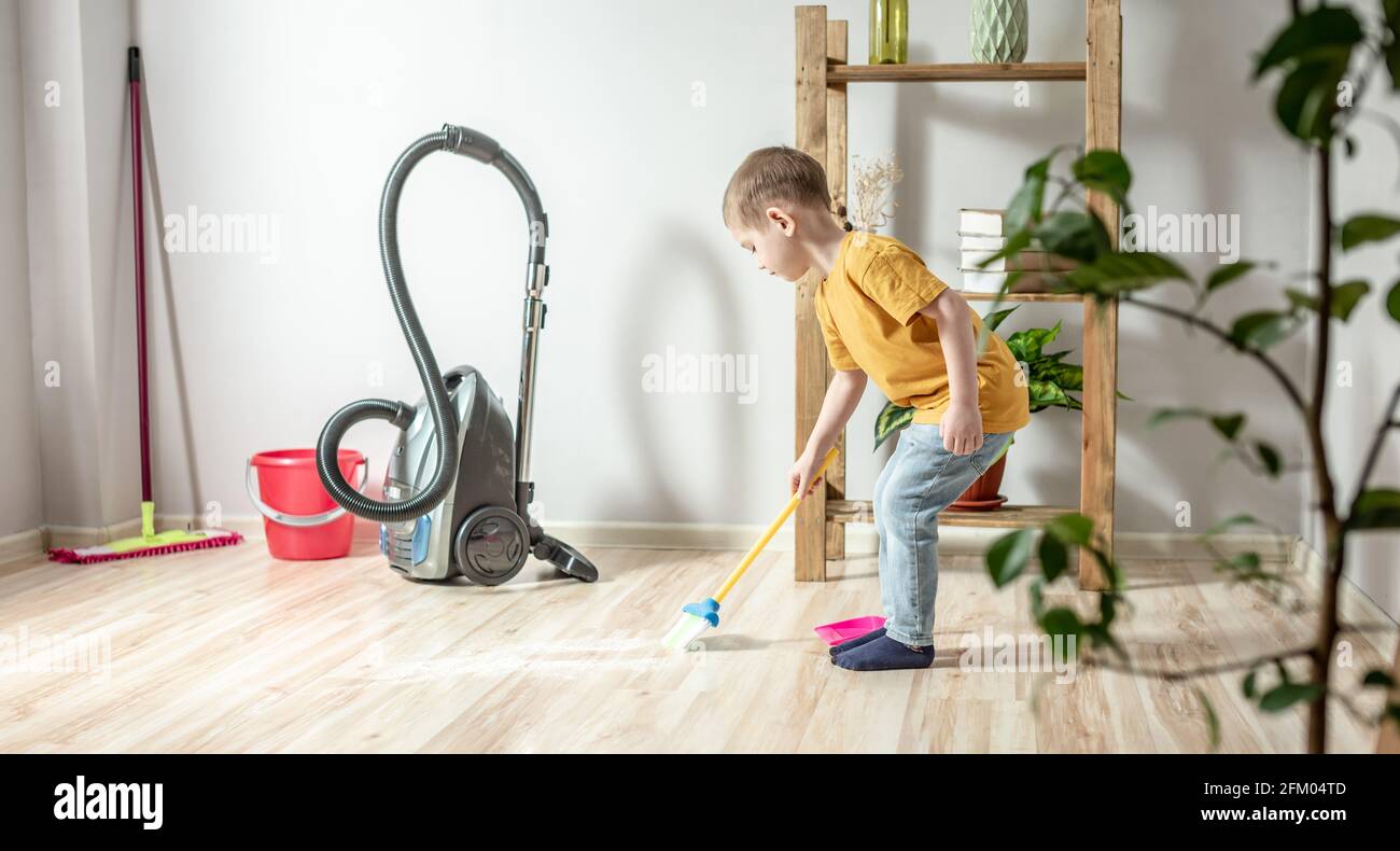 A cute little boy is sweeping the trash from the floor with a broom to ...