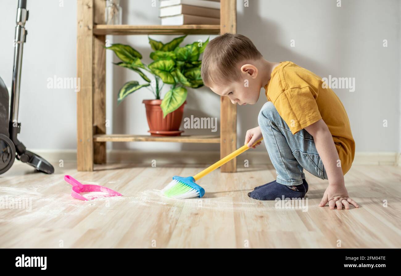 A cute little boy is sweeping the trash from the floor with a broom to ...
