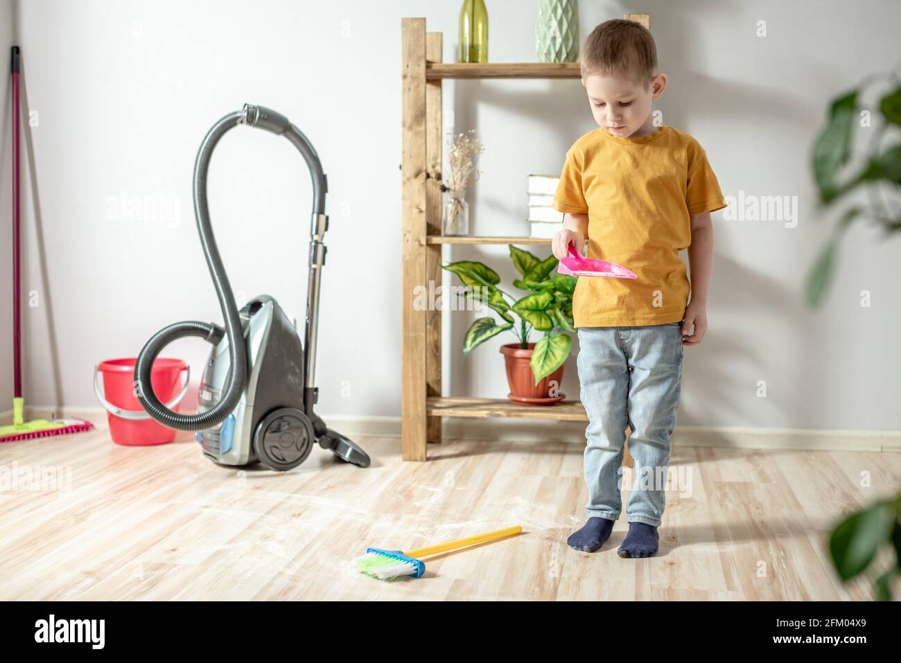 A cute little boy is sweeping the trash from the floor with a broom to ...