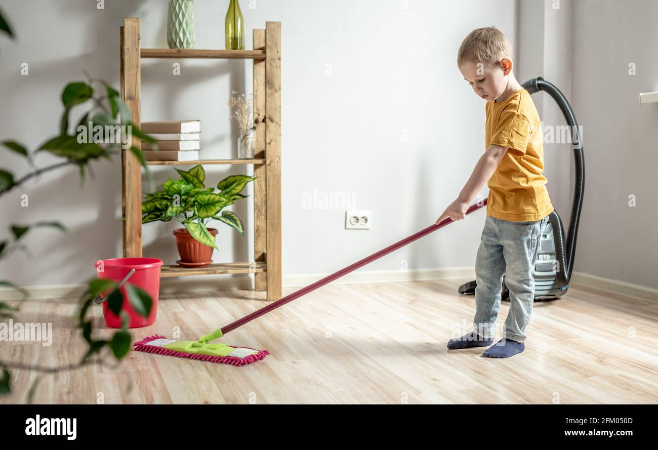 A little boy is cleaning the floor of a room using a mop. Concept of ...