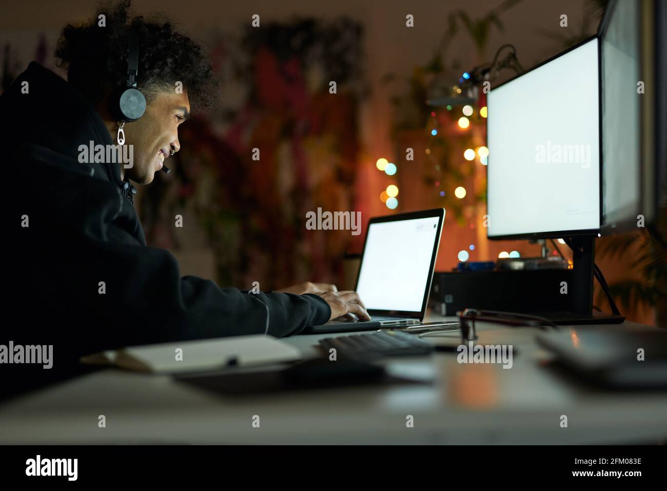 Night shift. Smiling young guy wearing headset sitting at the table in ...