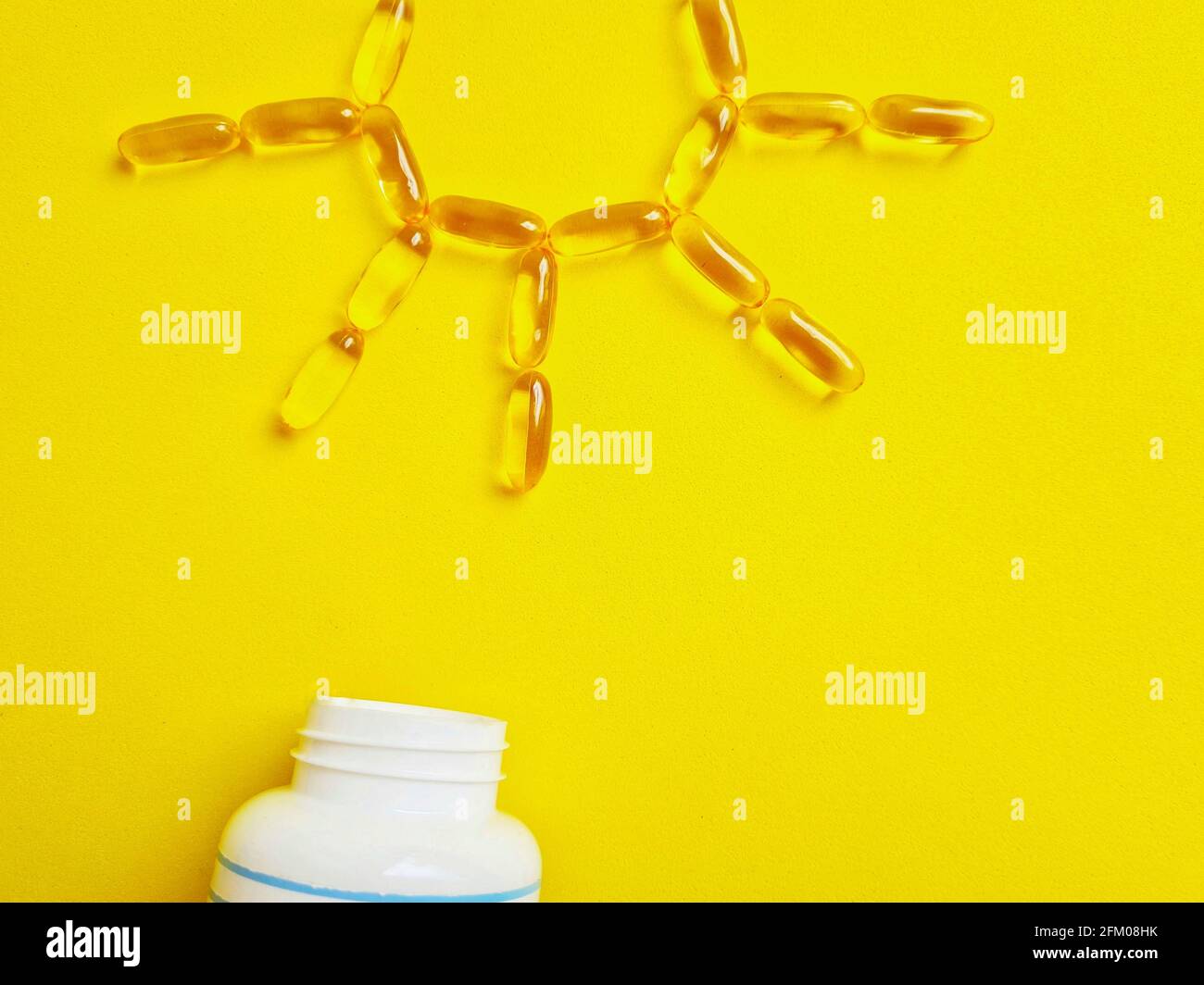 Sun created with dietary supplement capsules over a bottle on a yellow ...