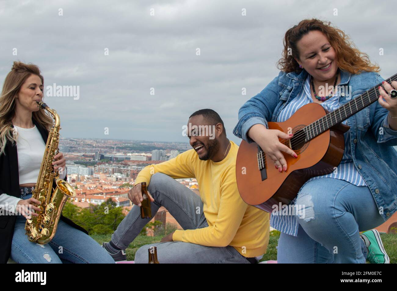 Happy interracial friends sitting in a park playing saxophone and ...