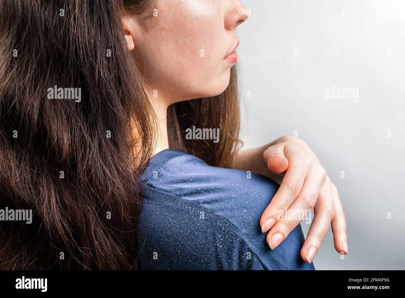 A brunette woman brushes dandruff off her shoulder with her hand ...