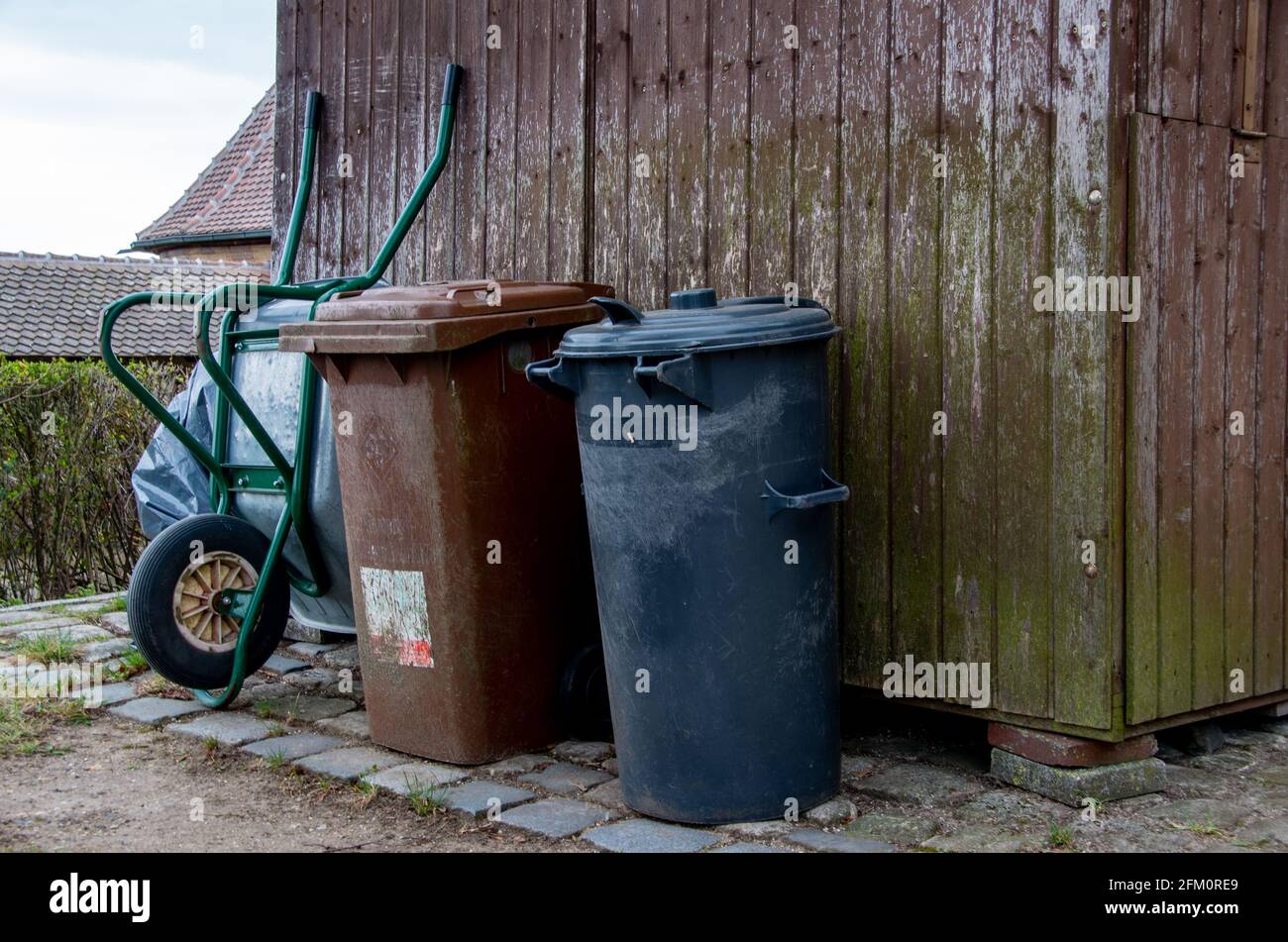 Garbage cans and a wheelbarrow lean against a wooden shed Stock Photo ...