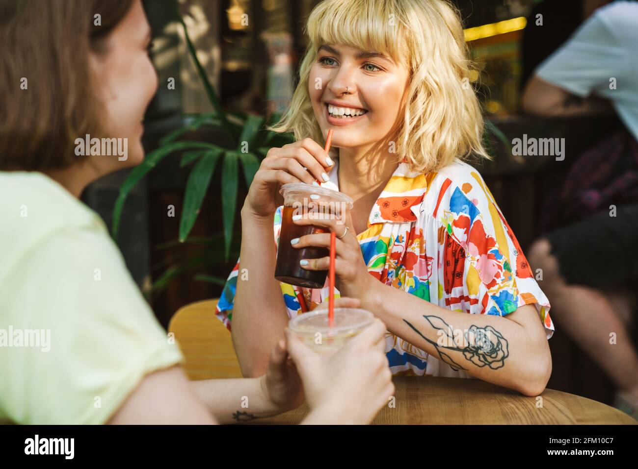Image of cheerful young two women laughing and drinking soda while ...