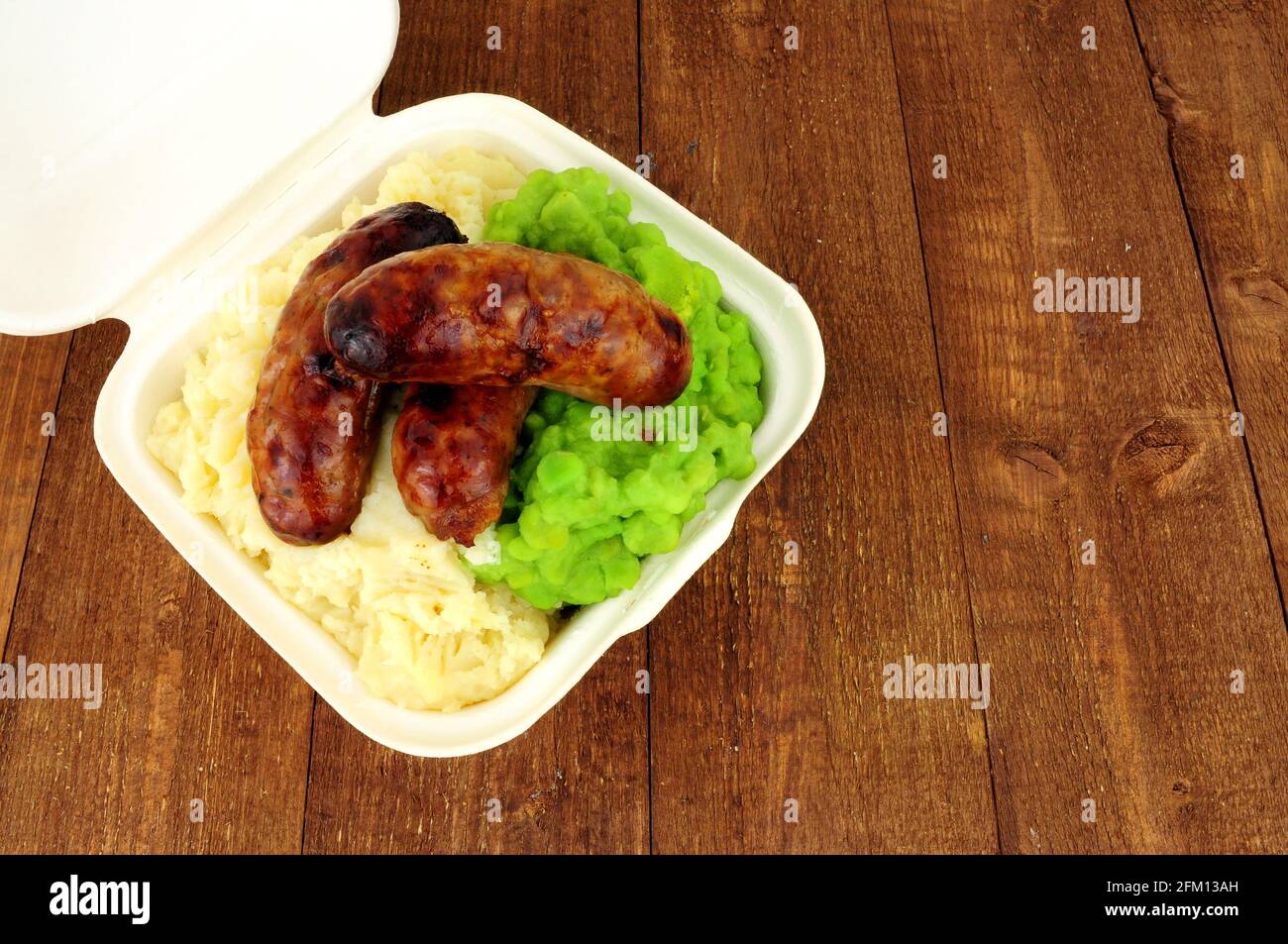 Sausages and mashed potato with mushy peas meal in a take away box on a ...