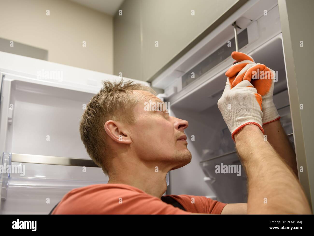The worker is fixing the built-in refrigerator in the kitchen furniture ...
