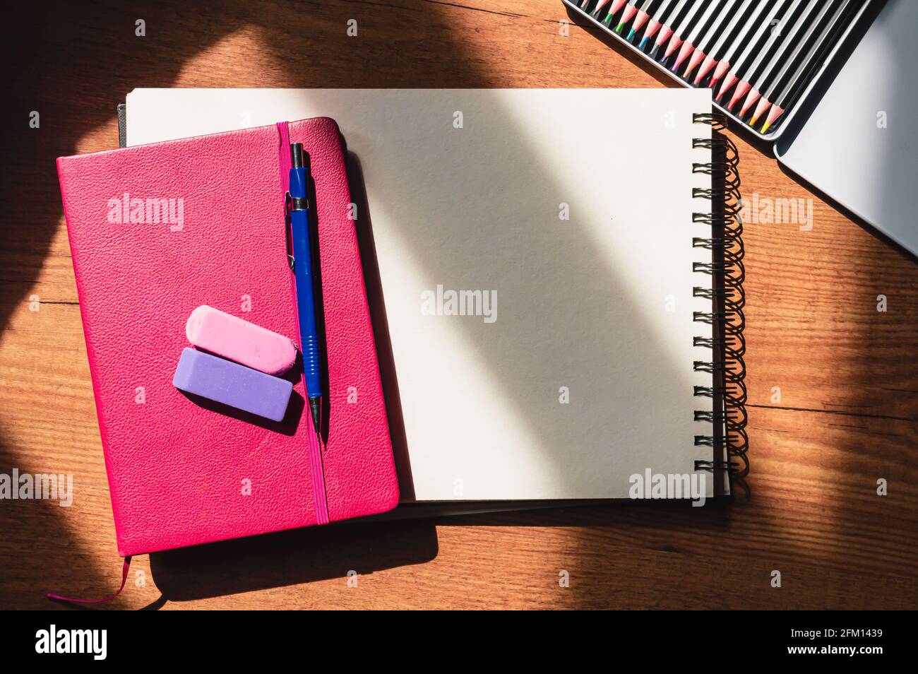 Overhead image of a pink notebook, two erasers, a filled pencil, a ...