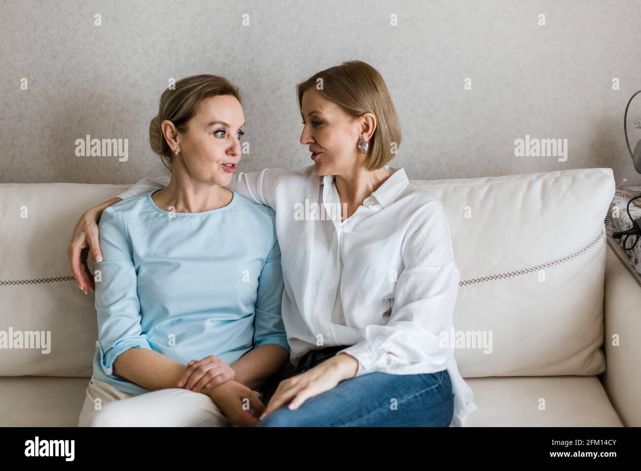 Two adult women are sitting on the couch talking to each other Stock ...