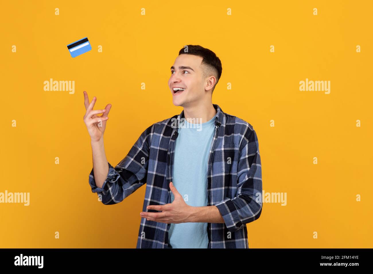 Attractive young guy throwing credit card up over orange studio ... Attractive young guy throwing credit card up over orange studio ...