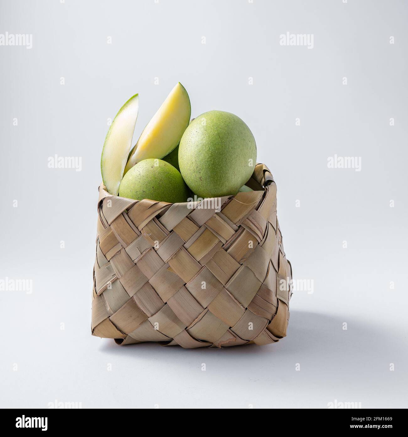 raw mangos or aam or green mangos in a wooden basket with mango leaves ...