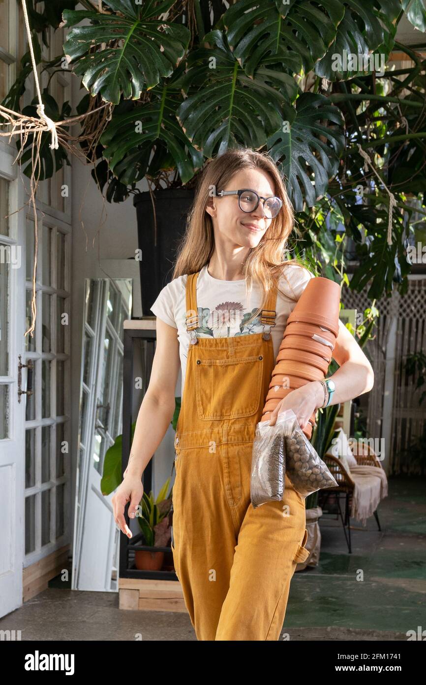 Young gardener girl in greenhouse carry pots and rocks for replanting ...