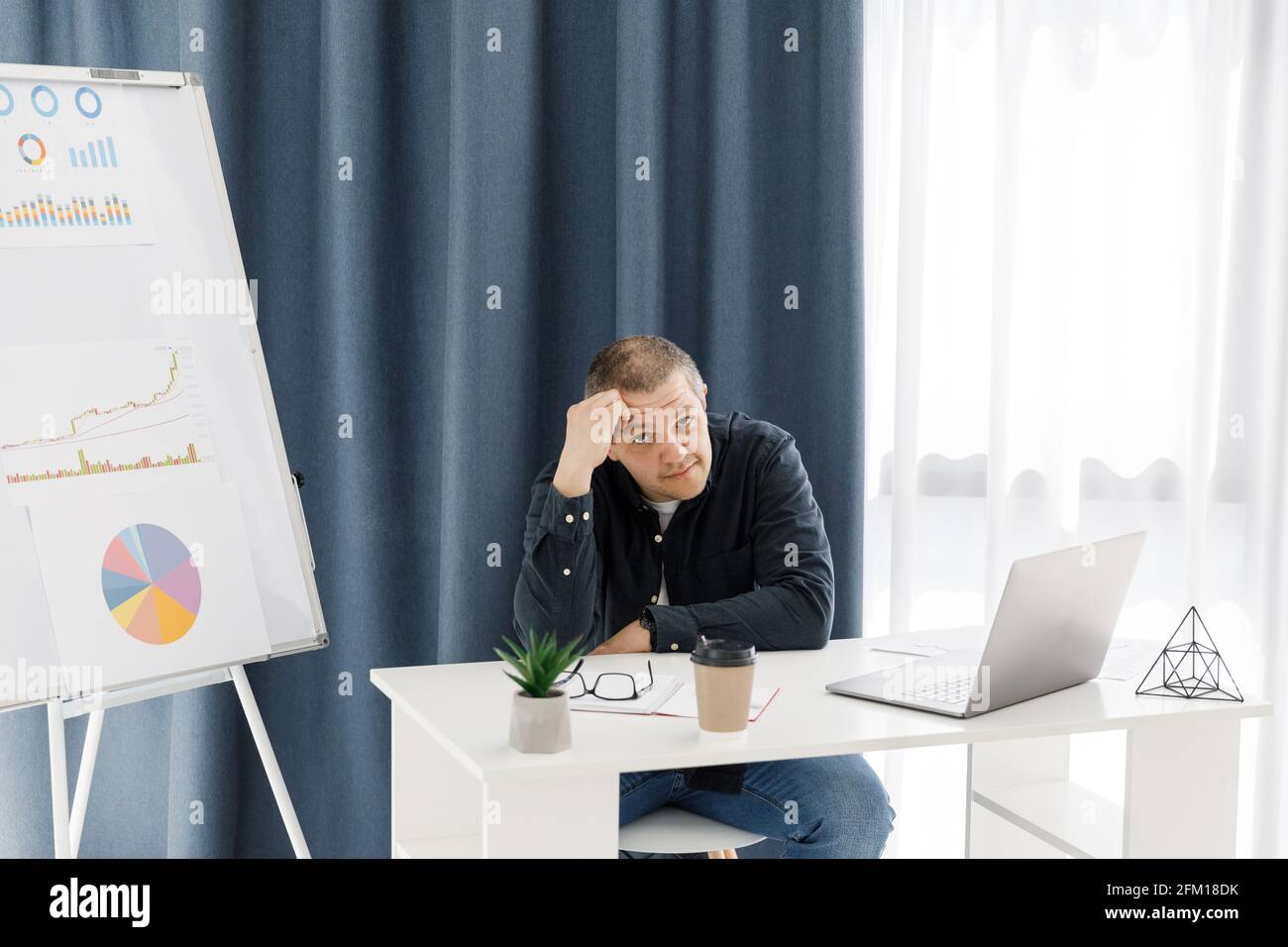 A man dressed in casual clothes works in the office with a laptop and ...