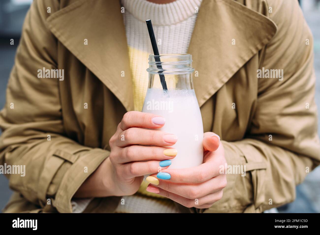A young woman drinks a milkshake outdoors from a stylish glass jar with ...