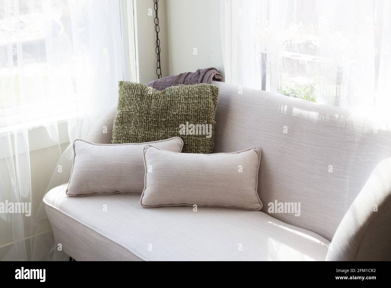 A loveseat next to windows with sun filtering through sheer white ...