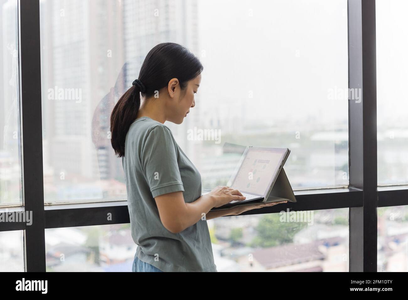 Woman standing next to window holding laptop computer Stock Photo - Alamy
