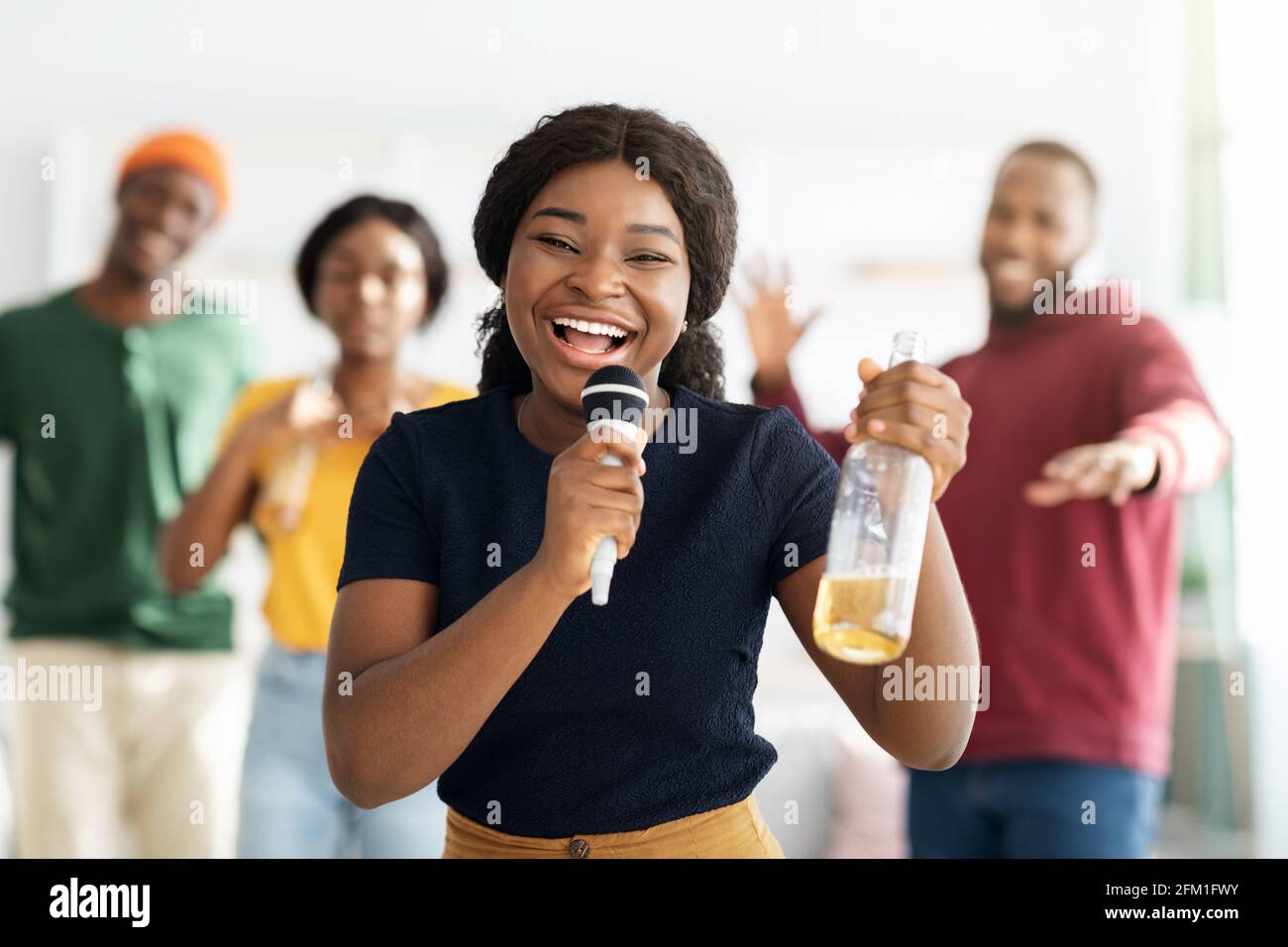 Positive black lady with bottle of beer singing karaoke Stock Photo - Alamy
