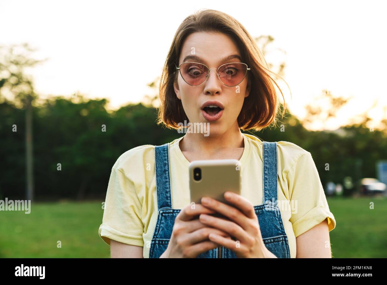 Image of astonished nice woman expressing surprise and using cellphone ...