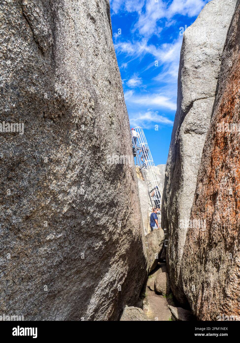 Granite boulders and tourists climbing caged ladder on Granite Skywalk ...