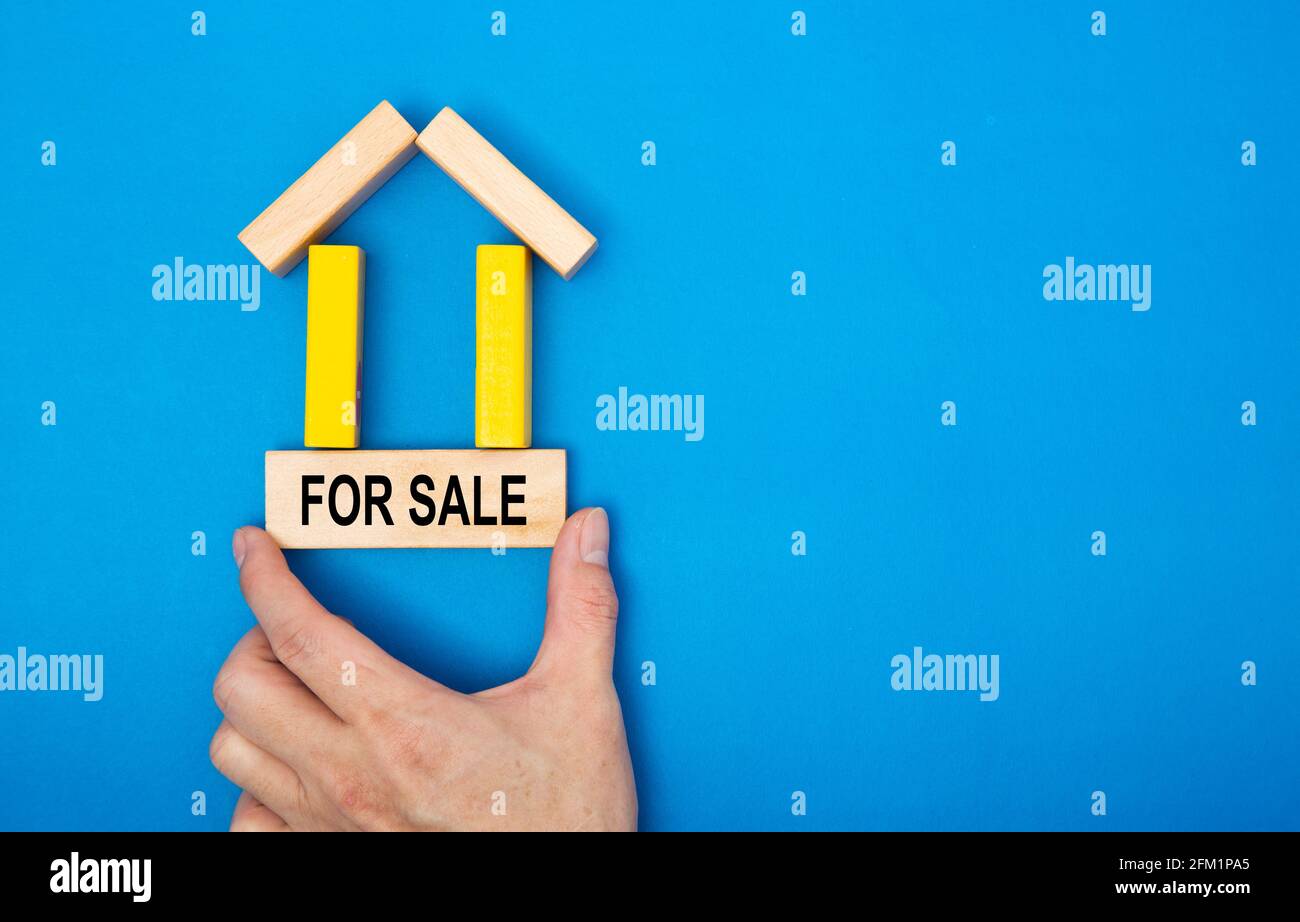 Male hand placing a Buy/Sell sign in a house made of wooden blocks in a ...