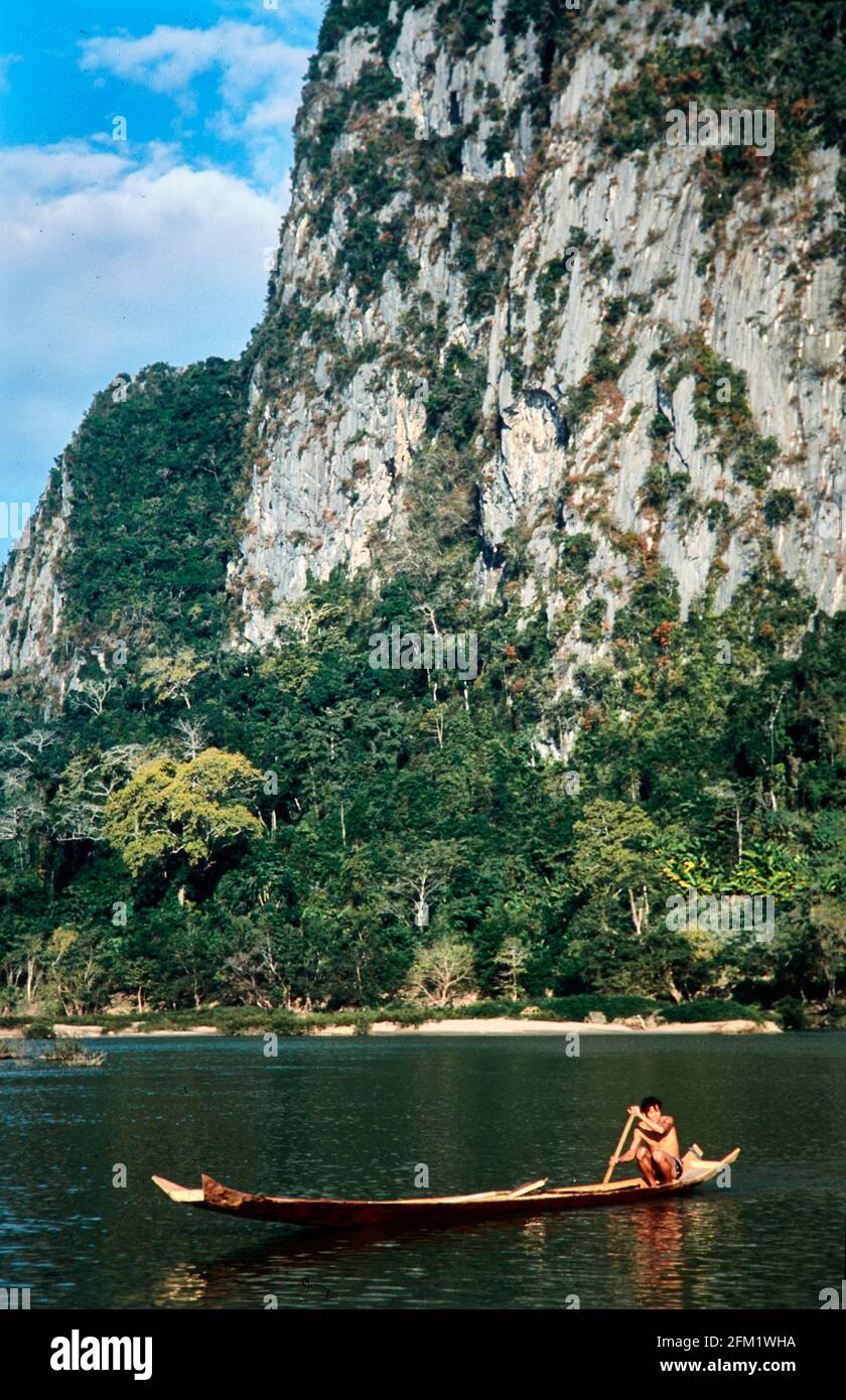 A man rowing a pirogue in front of rugged cliffs on the Nam Ou. 01/1997 ...