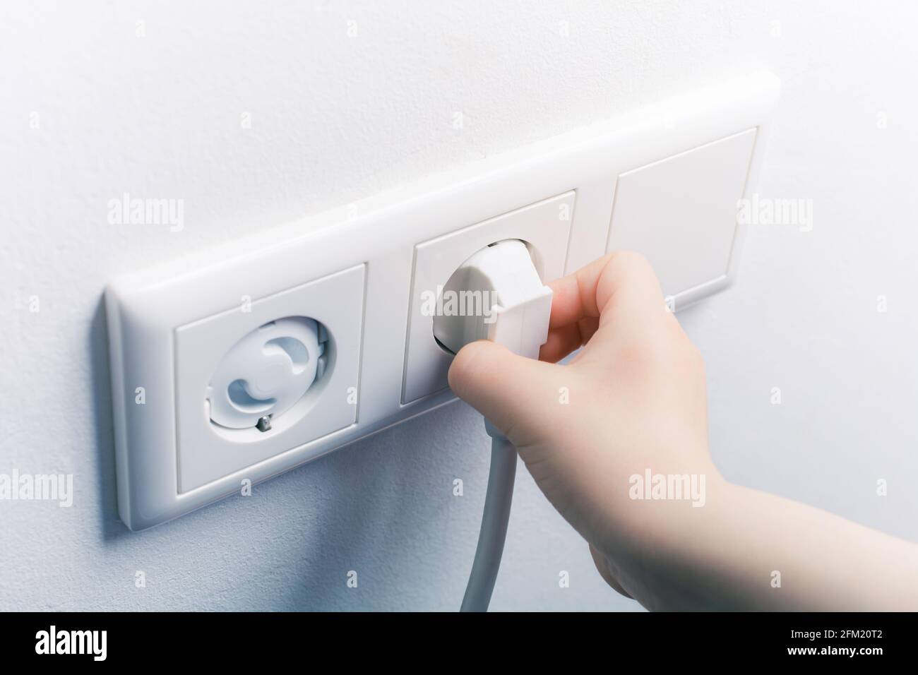 Child Hand Pulling A Power Cord Out Of Wall Socket With Safety Plugs ...