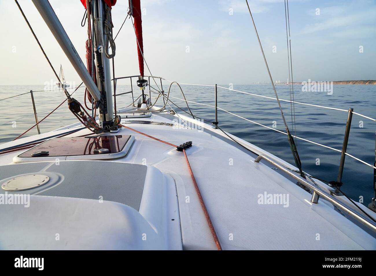 Side view of yacht sailing in blue sea with land visible from the right ...