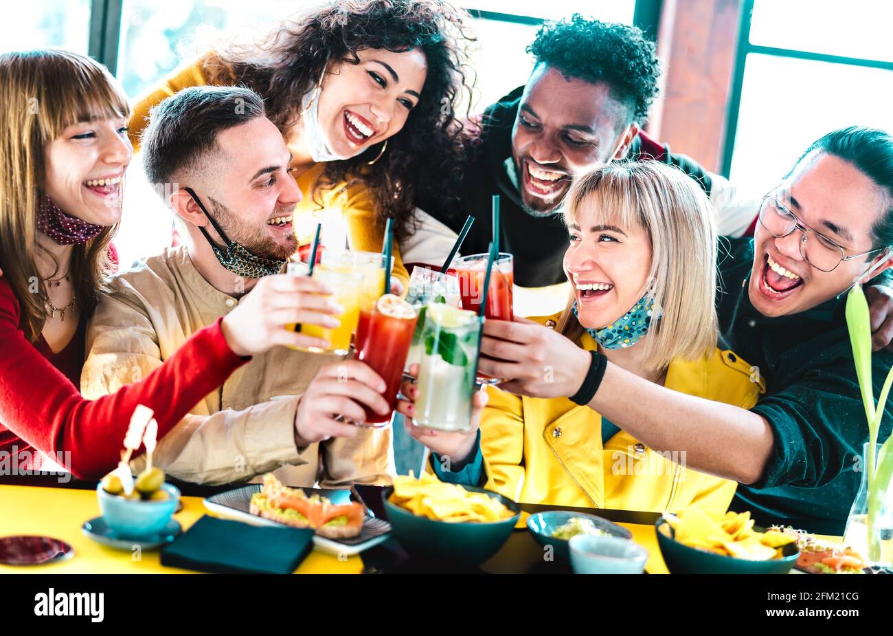 Happy multiracial friends toasting drinks with open face masks - New ...