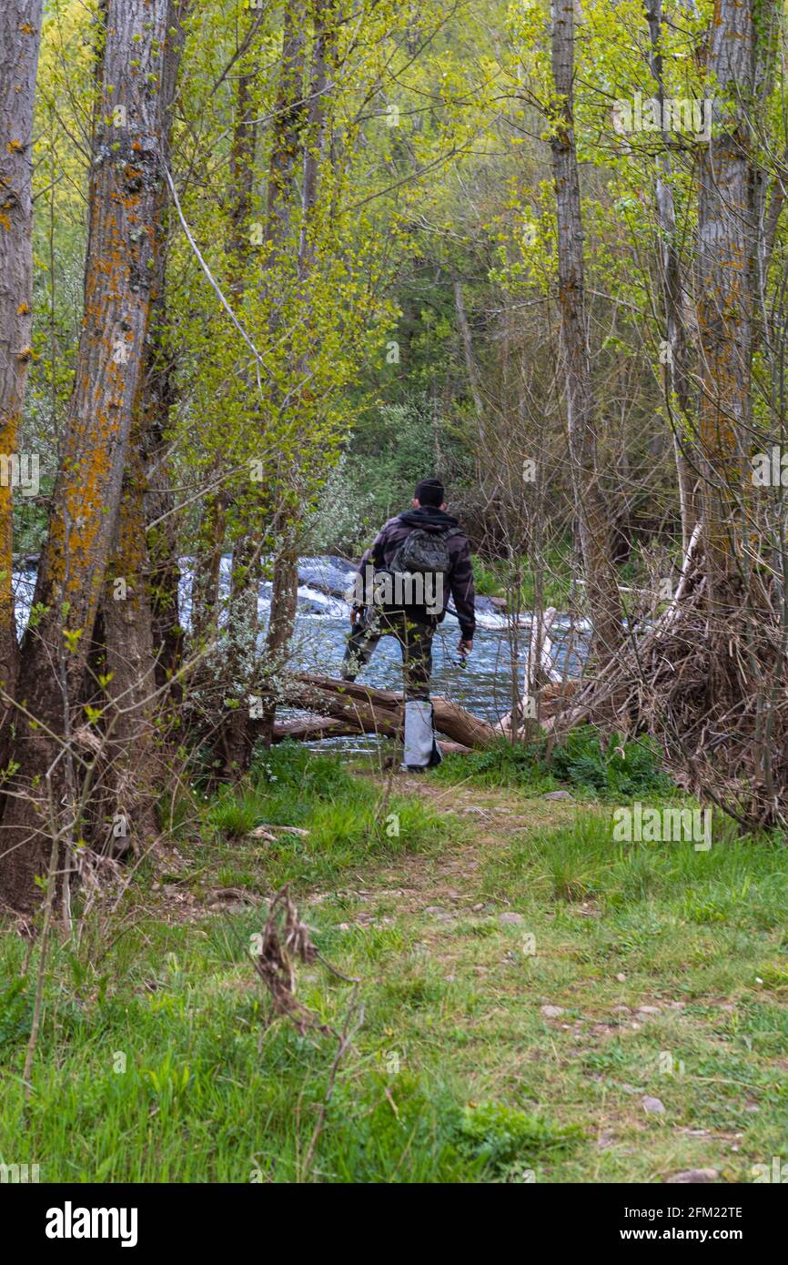 Teenager with fishing suit, rod and tools crossing some branches of the ...