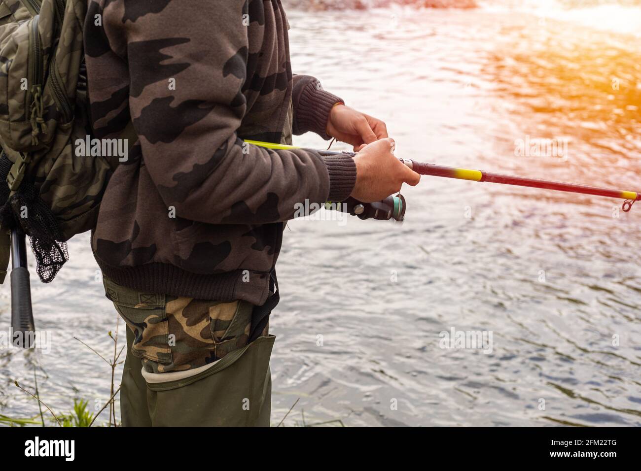 Detail of a fisherman in camouflage clothing high rubber boots holding ...