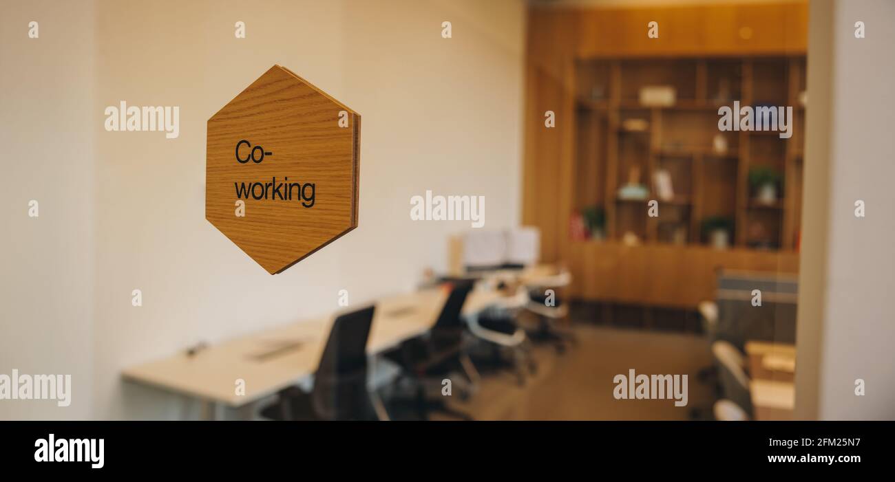 Co-working sign board on glass with tables and chairs in background ...
