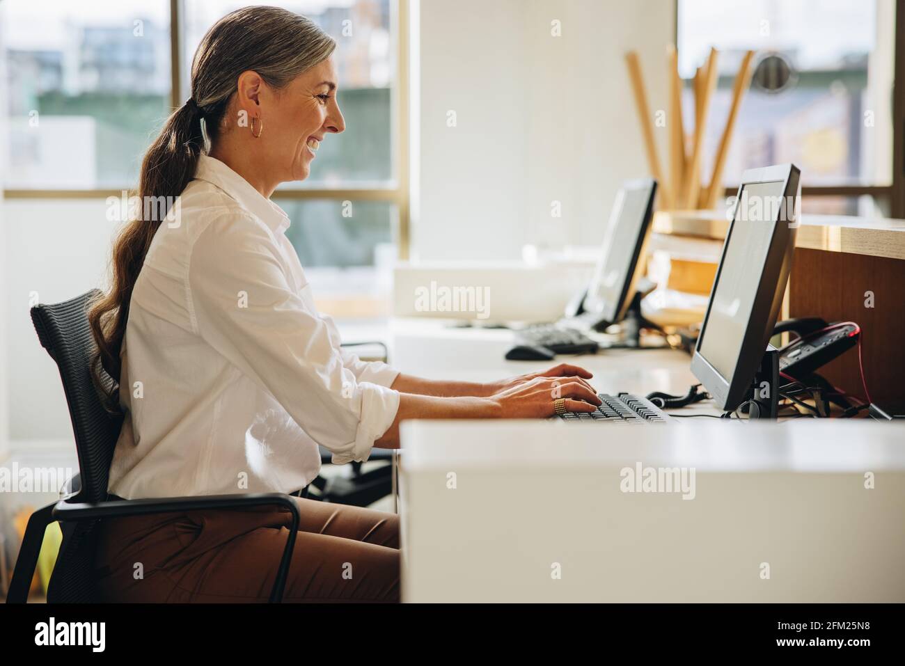 Side view of smiling woman sitting at desk and typing on computer in ...