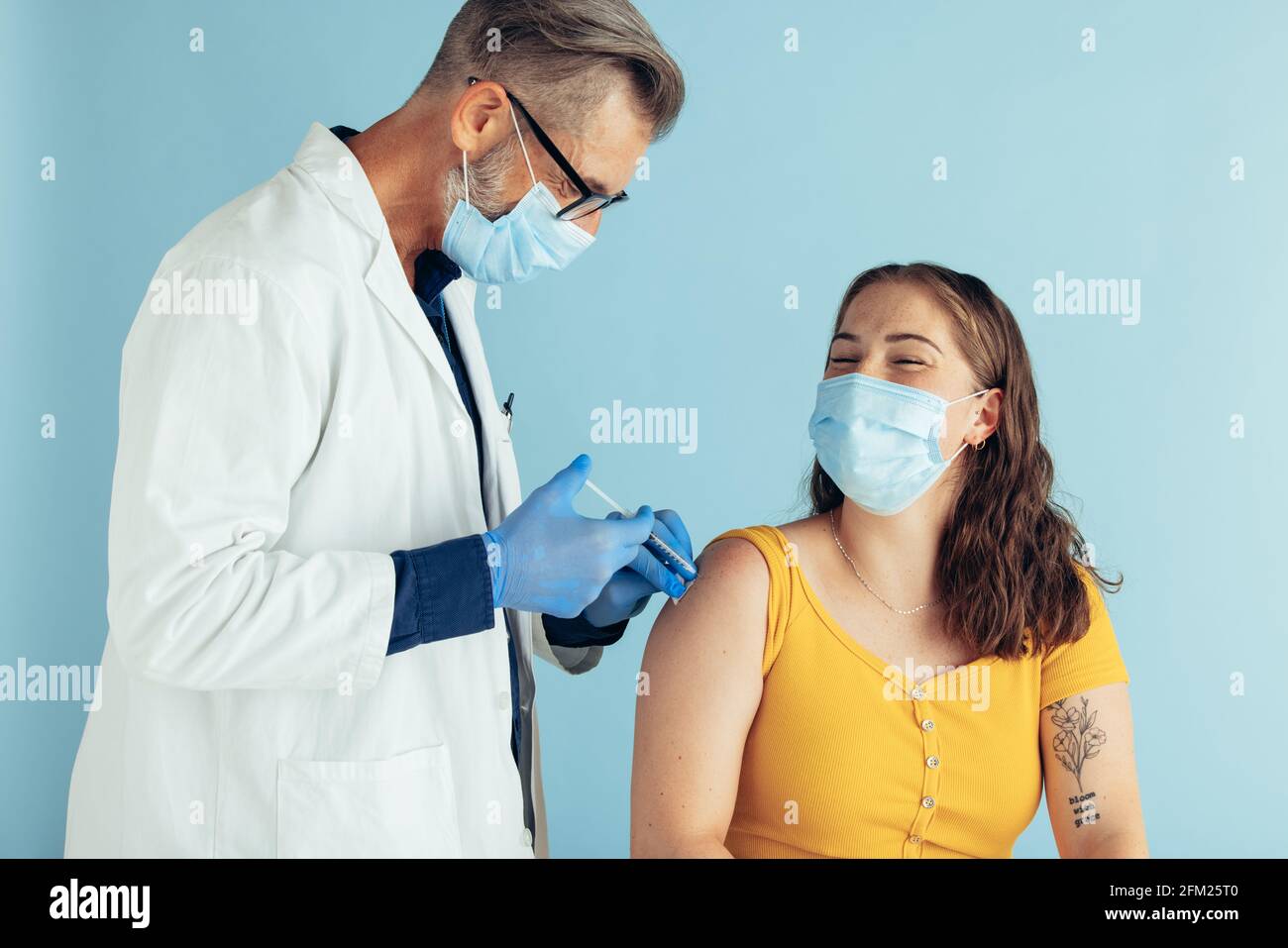 Woman wearing face mask closing her eyes while getting vaccine on her ...