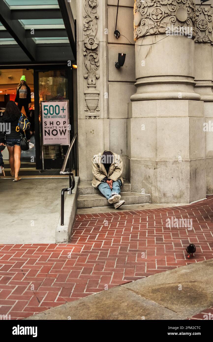 Homeless man sitting outside a luxury shopping mall as people walk by ...