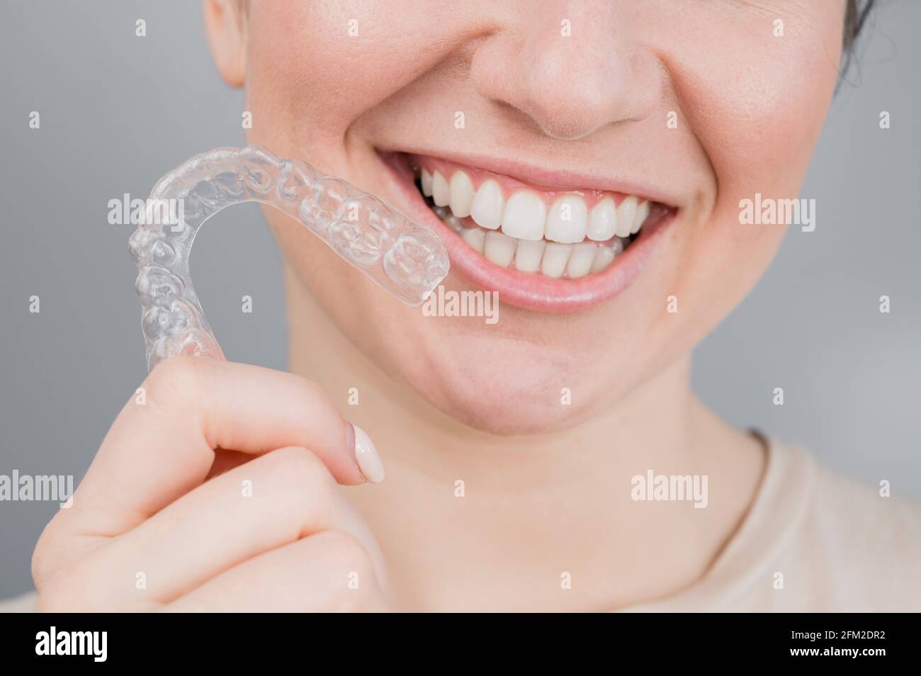 Close-up portrait of a woman holding a plastic transparent retainer. A ...