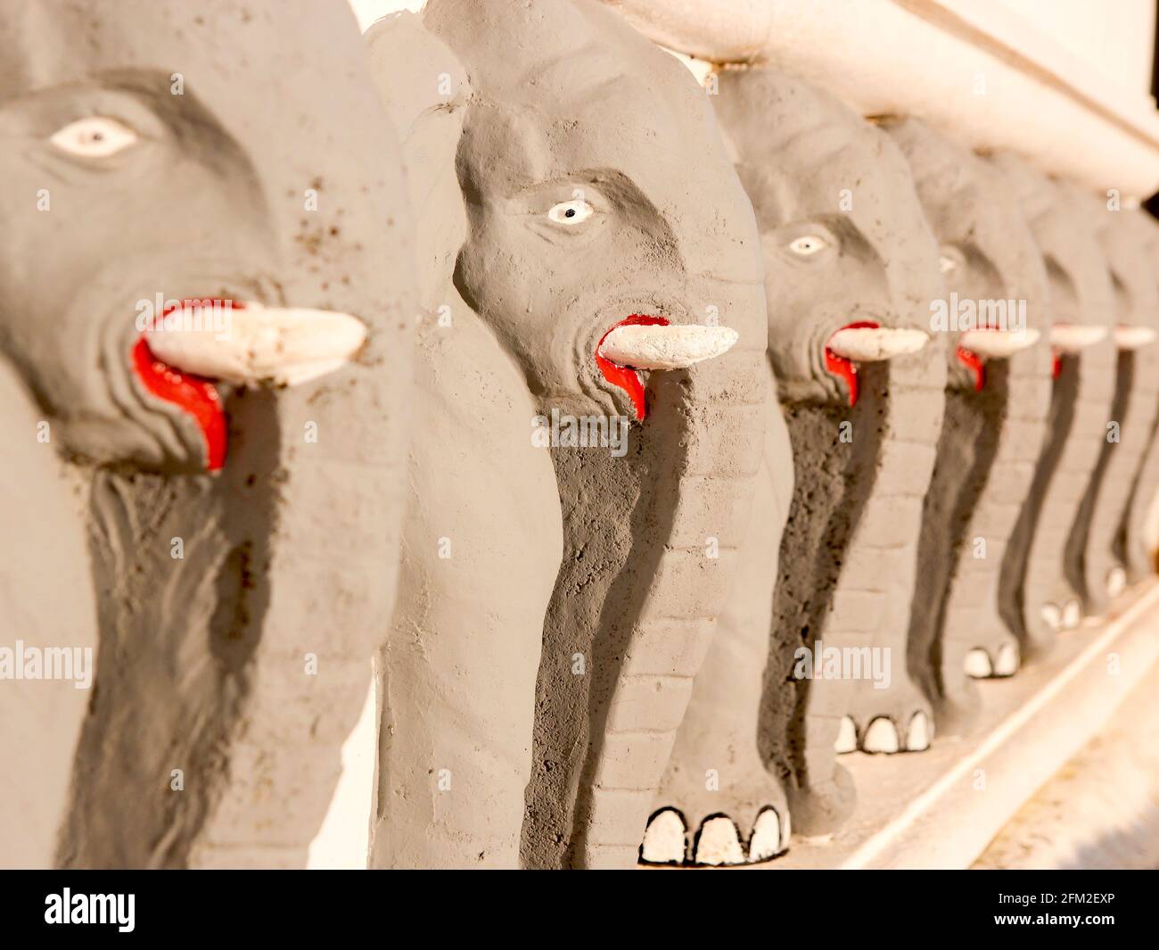 Along the facade of a building is a row of concrete, painted elephants ...