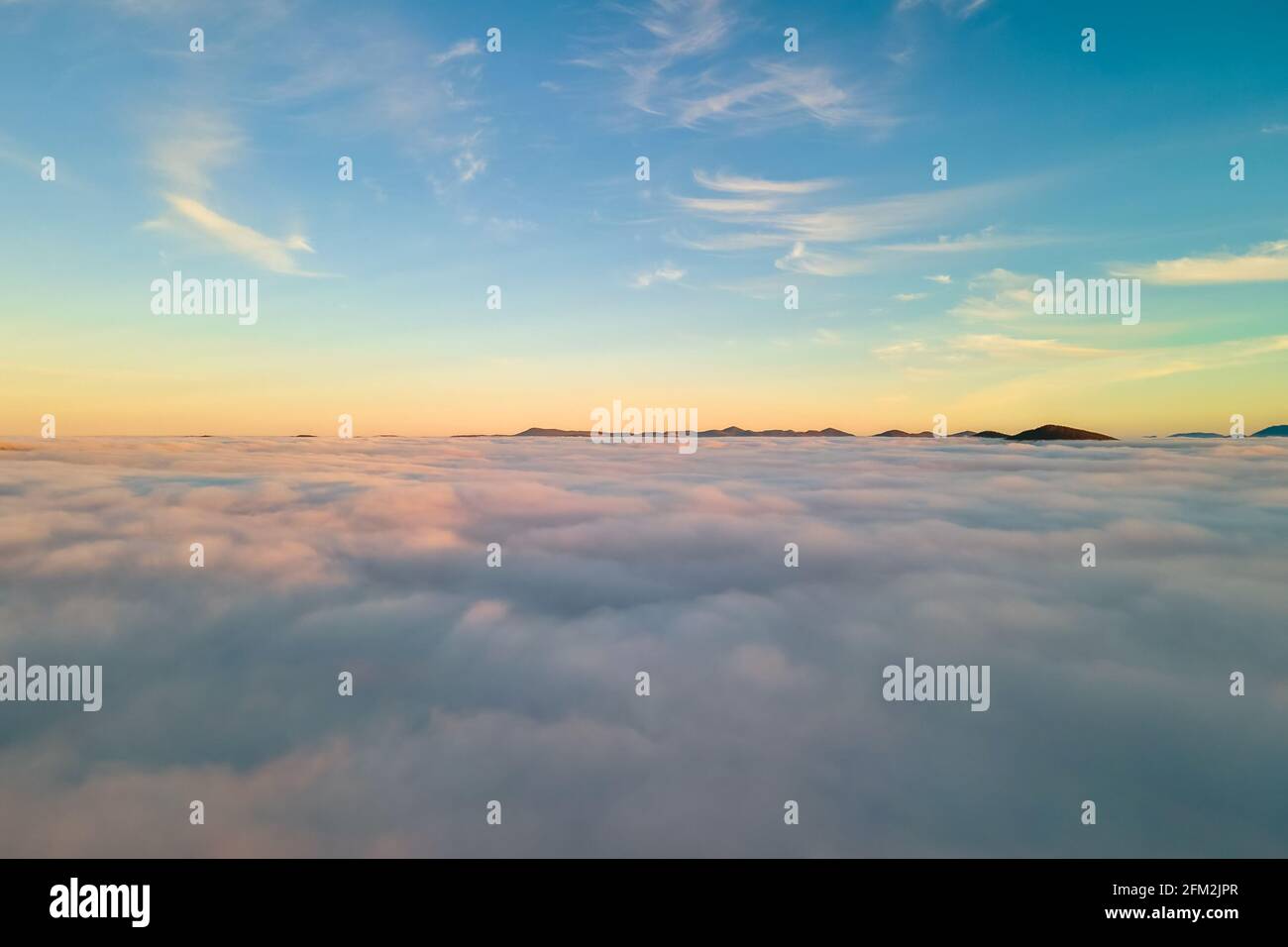 Aerial view of vibrant sunset over white dense clouds with distant dark ...