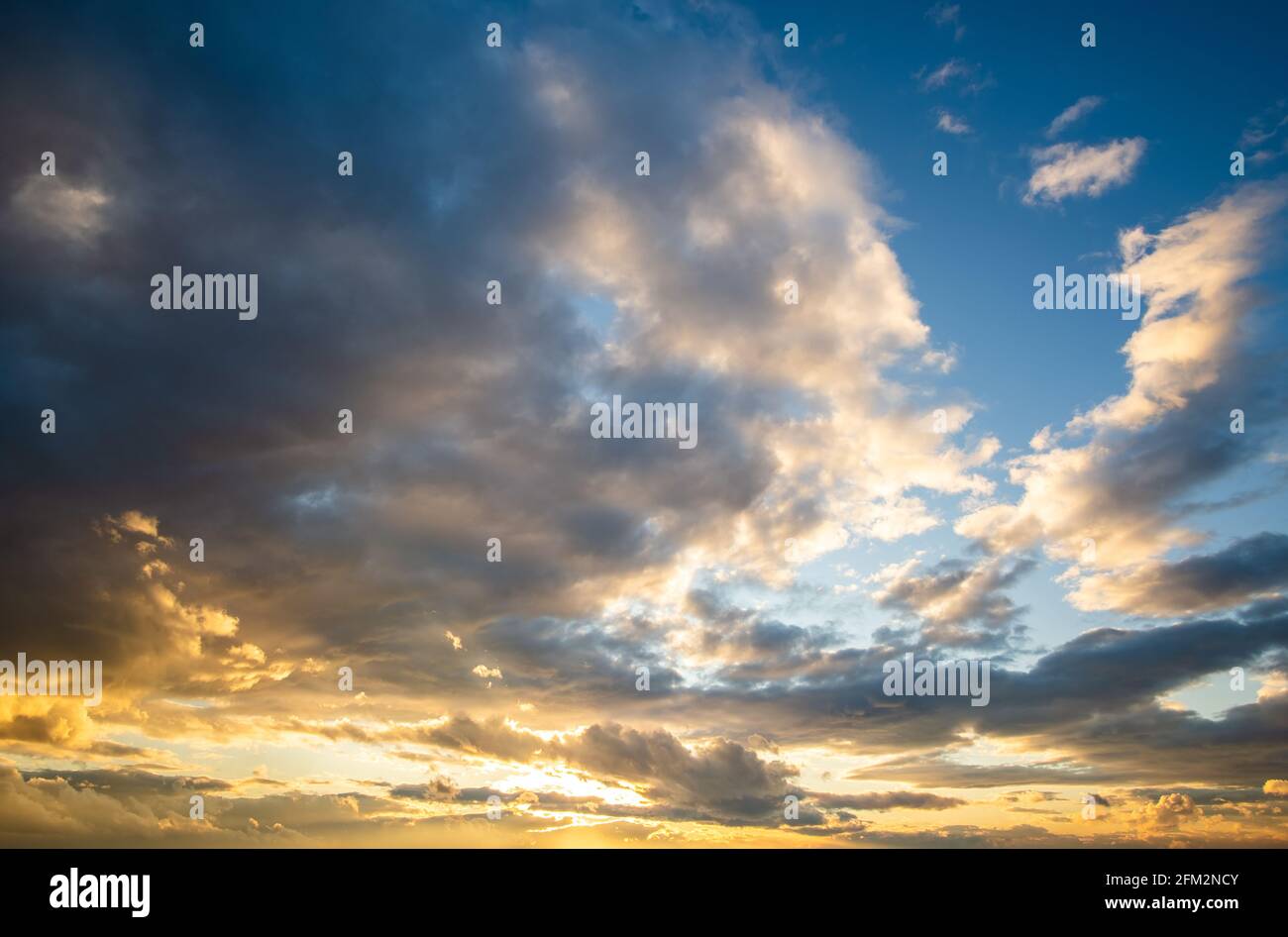 Dramatic sunset landscape with puffy clouds lit by orange setting sun ...